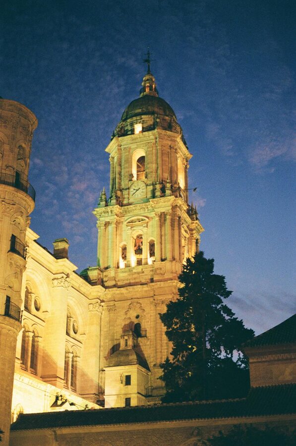 Illuminated M&aacute;laga Cathedral tower at twilight against a dusky sky