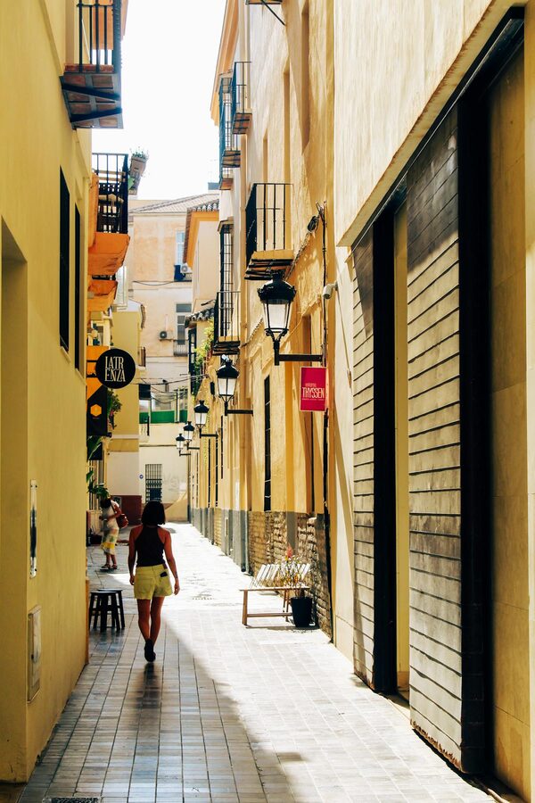 Person walking through a sunlit alleyway in M&aacute;laga with classic architecture