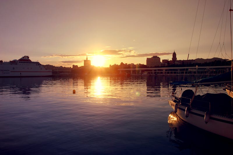Sunset scene over Malaga harbor with boats and reflections on the water