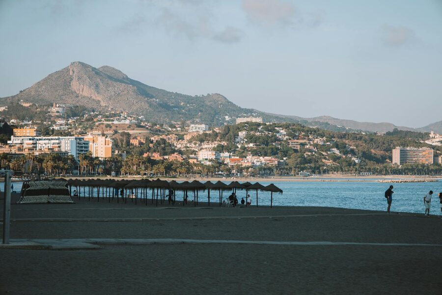 People on Malagueta Beach in Malaga with mountain backdrop during sunset
