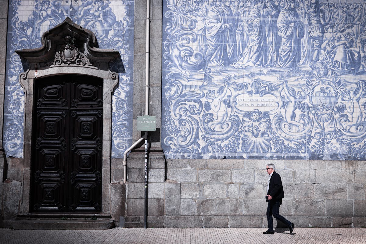 A man walks along a large blue and white azulejo tile wall in Porto capturing Portuguese art and culture