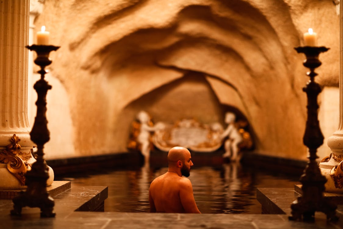 Man unwinding in a candlelit indoor bath with classical architecture