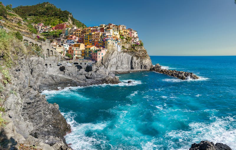 The village of Manarola perched on rocky cliffs above the deep blue Ligurian Sea under clear skies