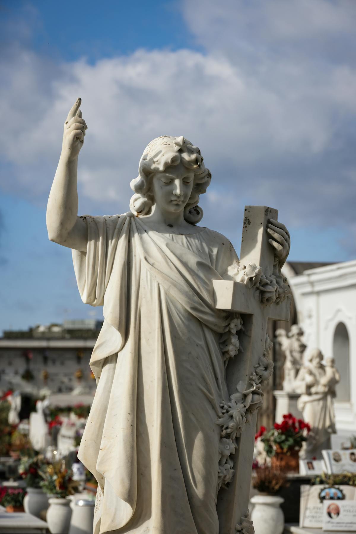 Marble cemetery statue holding a cross bathed in sunlight with trees in the background
