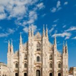 The intricate Gothic facade of the Milan Cathedral (Duomo di Milano) against a bright blue sky