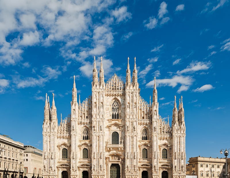 The intricate Gothic facade of the Milan Cathedral (Duomo di Milano) against a bright blue sky