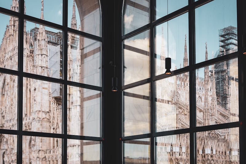 The Milan Cathedral facade reflected in the glass windows of a modern building