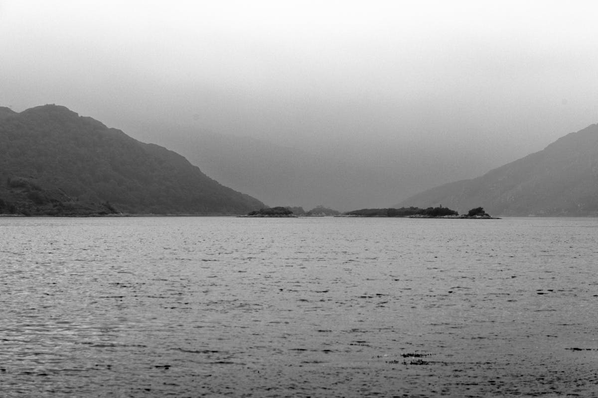 A misty morning scene at Lochailort in Scotland with calm waters reflecting the surrounding hills and soft grey clouds