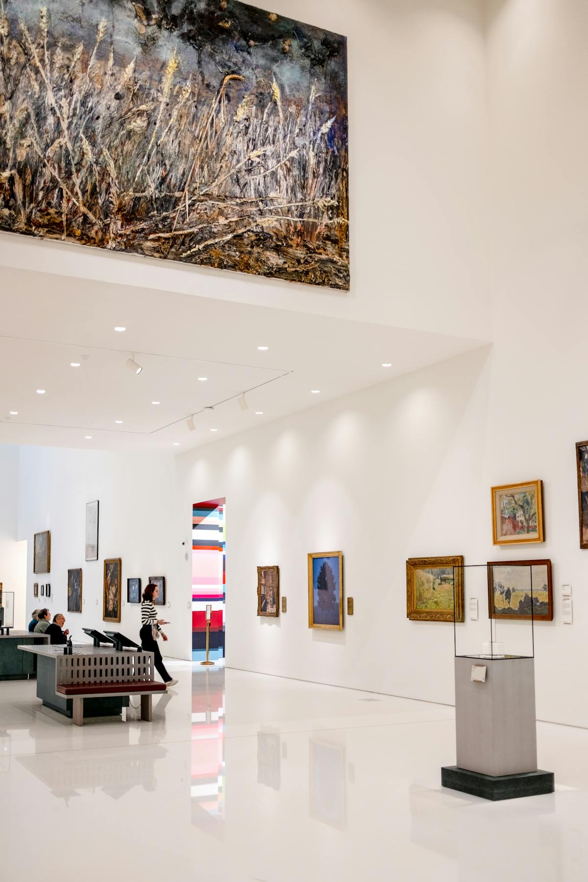 A modern art museum interior with visitors observing a diverse collection of paintings