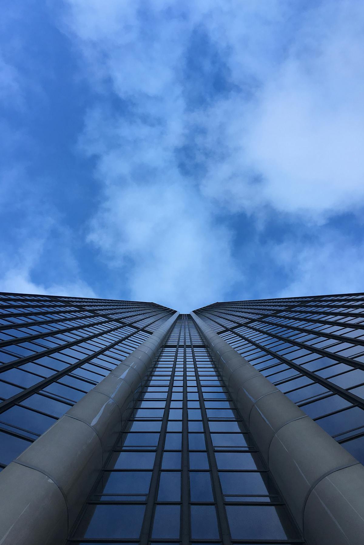 Looking up at Montparnasse Tower from street level with blue sky and clouds
