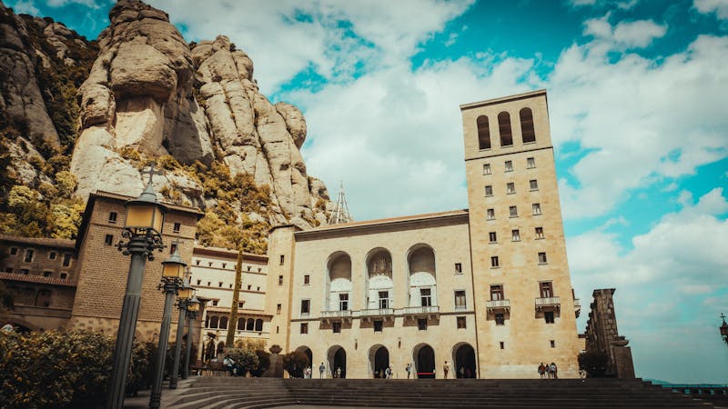 Montserrat Abbey buildings sitting at the base of towering rock formations with blue sky