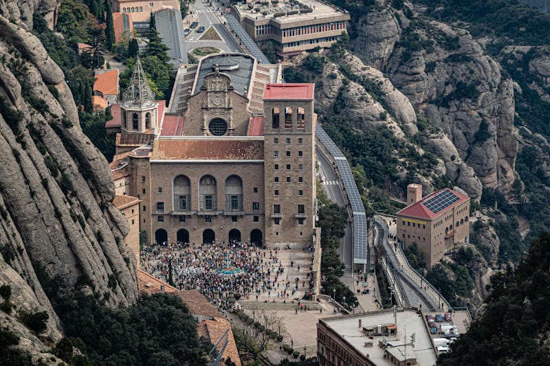 Aerial view of Montserrat Abbey surrounded by jagged rock formations and tourists