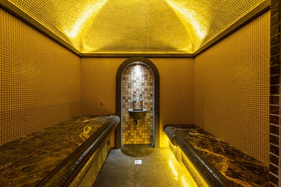 Elegant mosaic-decorated bathhouse interior with warm lighting and marble seats