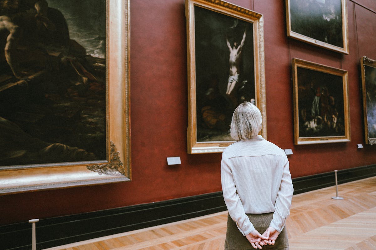 A woman observing paintings in a museum gallery from behind