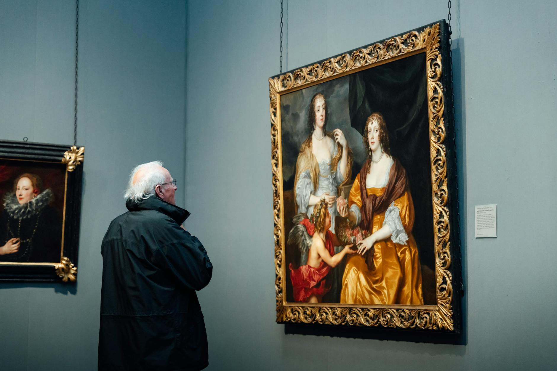 A senior man observes classical paintings in an art museum gallery