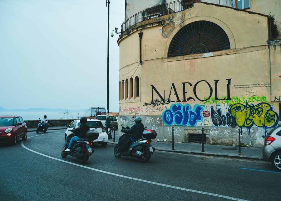 Street scene in Naples with scooters and cars against graffiti covered wall