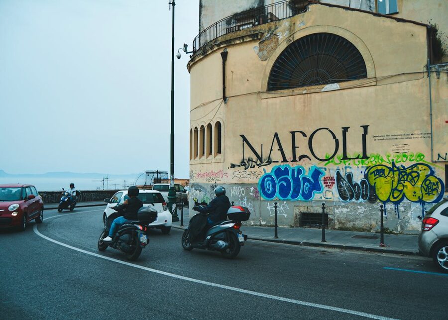 Street scene in Naples with scooters parked against a graffiti-covered wall