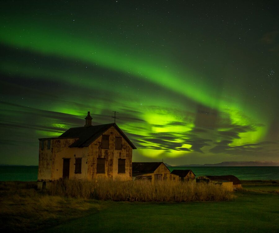 Northern lights illuminate an abandoned house on the coastline of KeflavÃ­k, Iceland under a starry n
