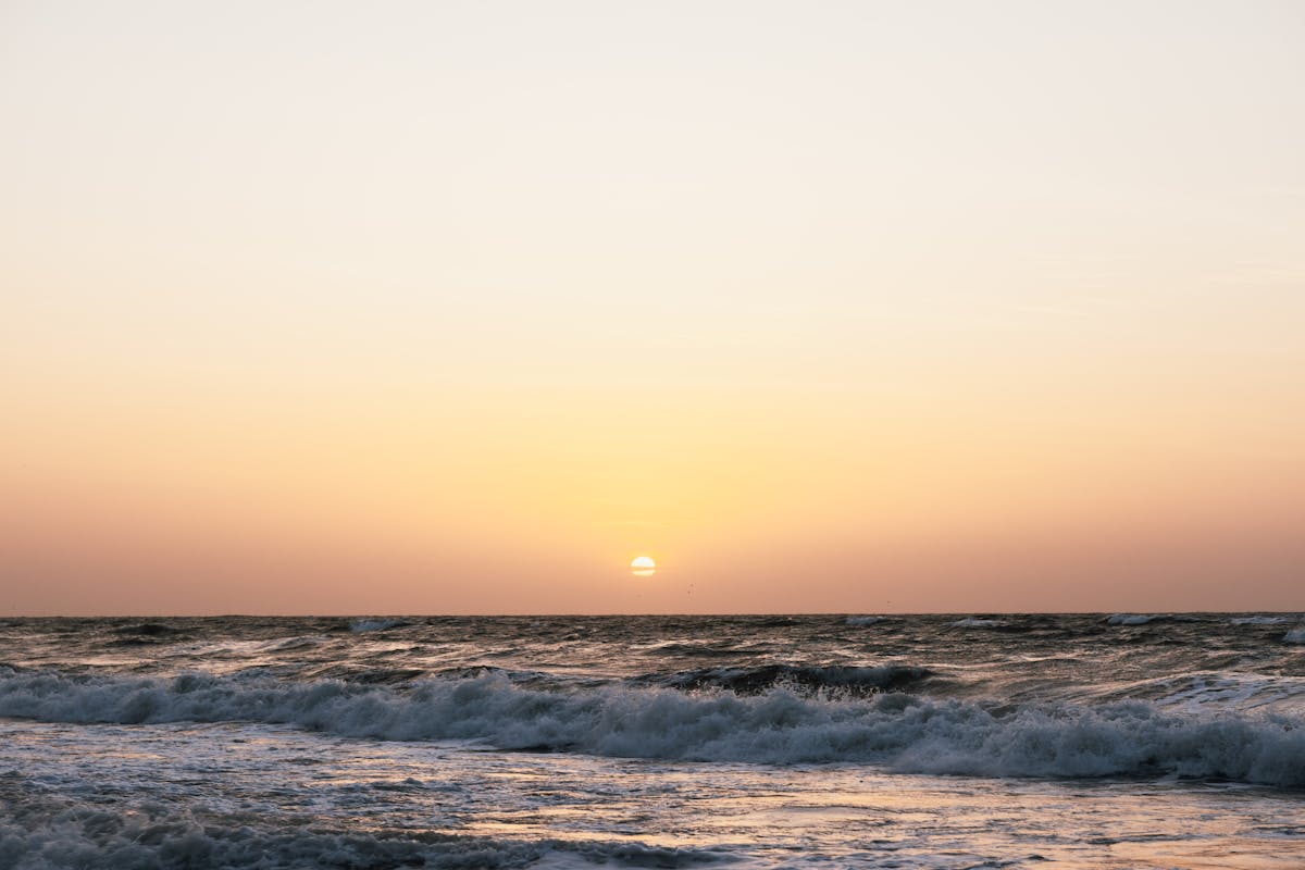 Sunset over the ocean with waves crashing on the shore under a golden sky