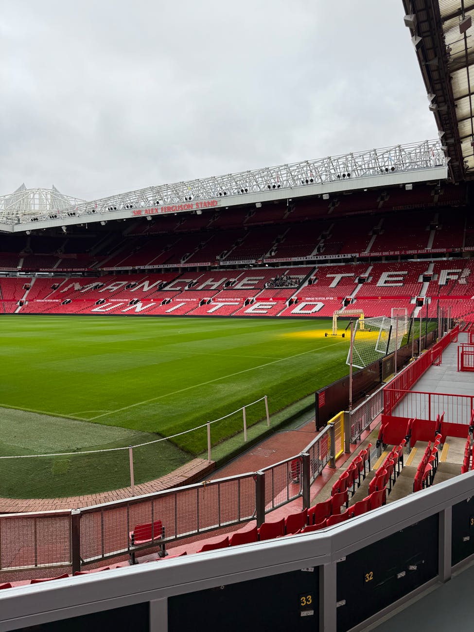 Wide view inside Old Trafford stadium showing the empty red seats and green pitch