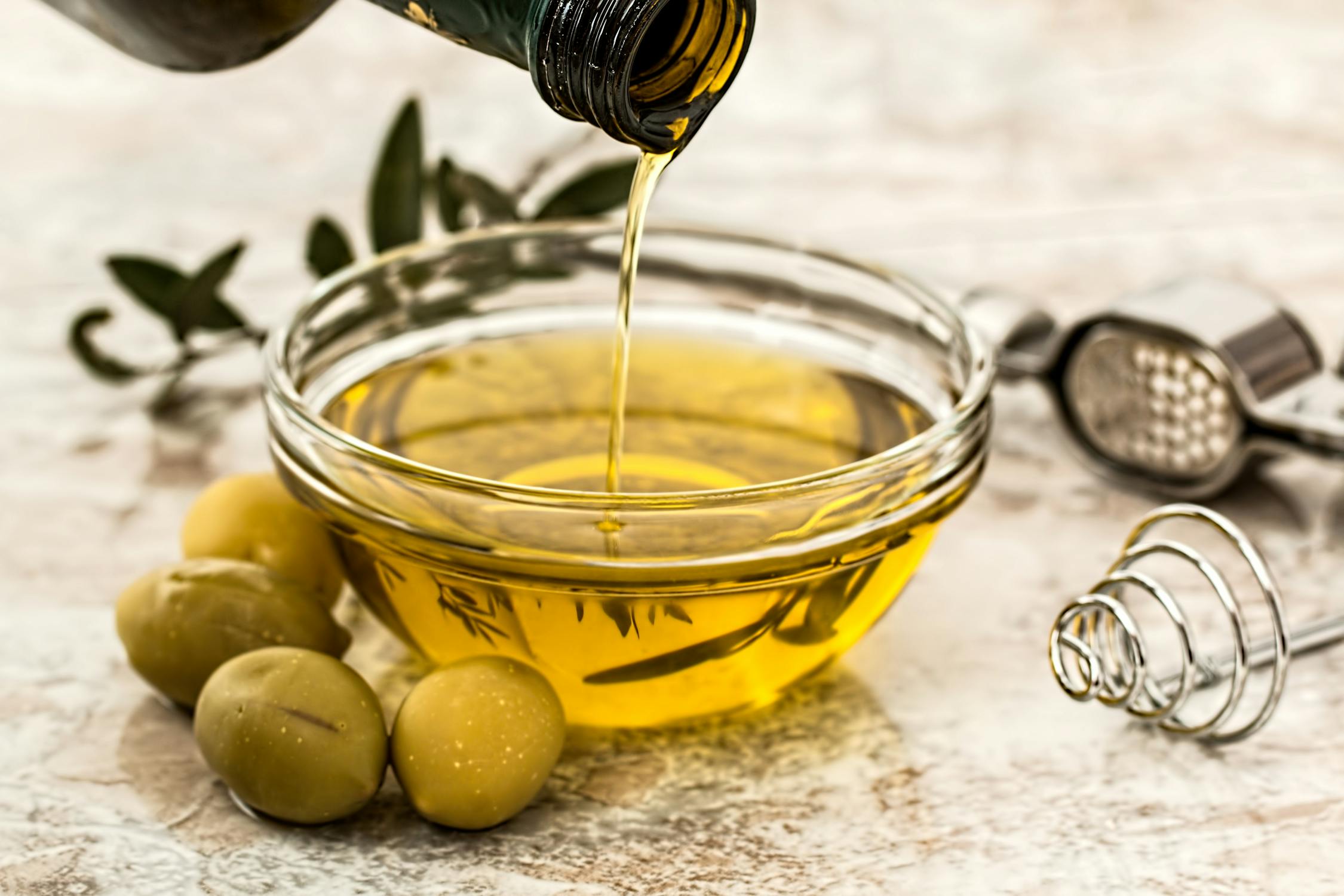 Olive oil being poured into a bowl surrounded by fresh olives