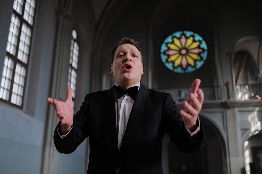 A singer performing passionately inside a church with stained glass windows behind them