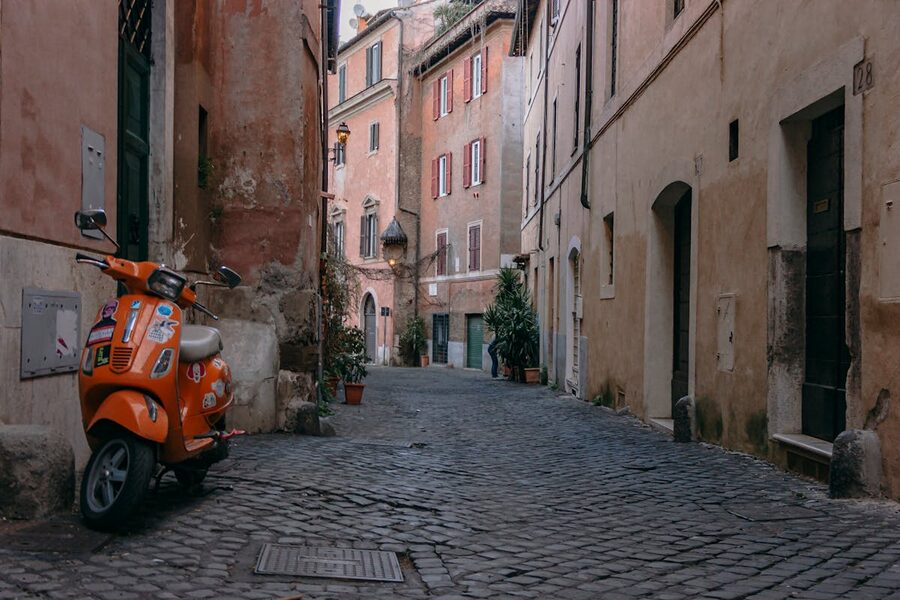 An orange Vespa scooter parked on a cobblestone street in Trastevere, Rome