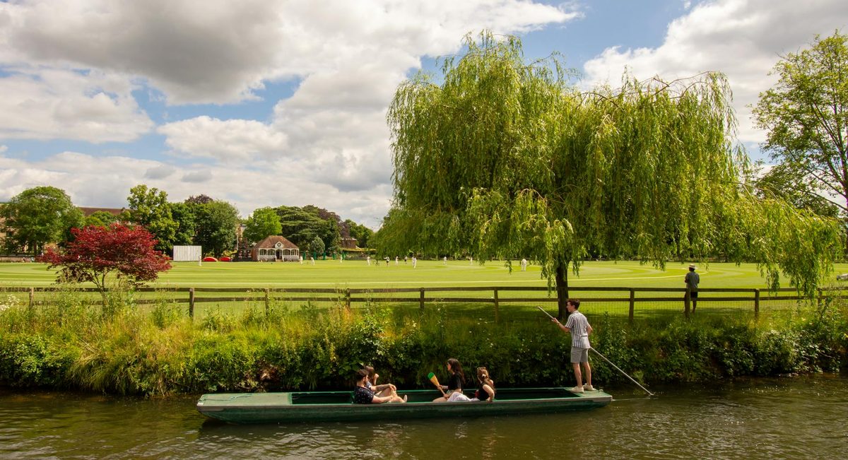 People punting on the river in Oxford with green scenery