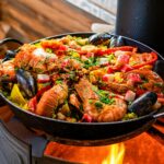 Seafood paella sizzling over an open flame outdoors