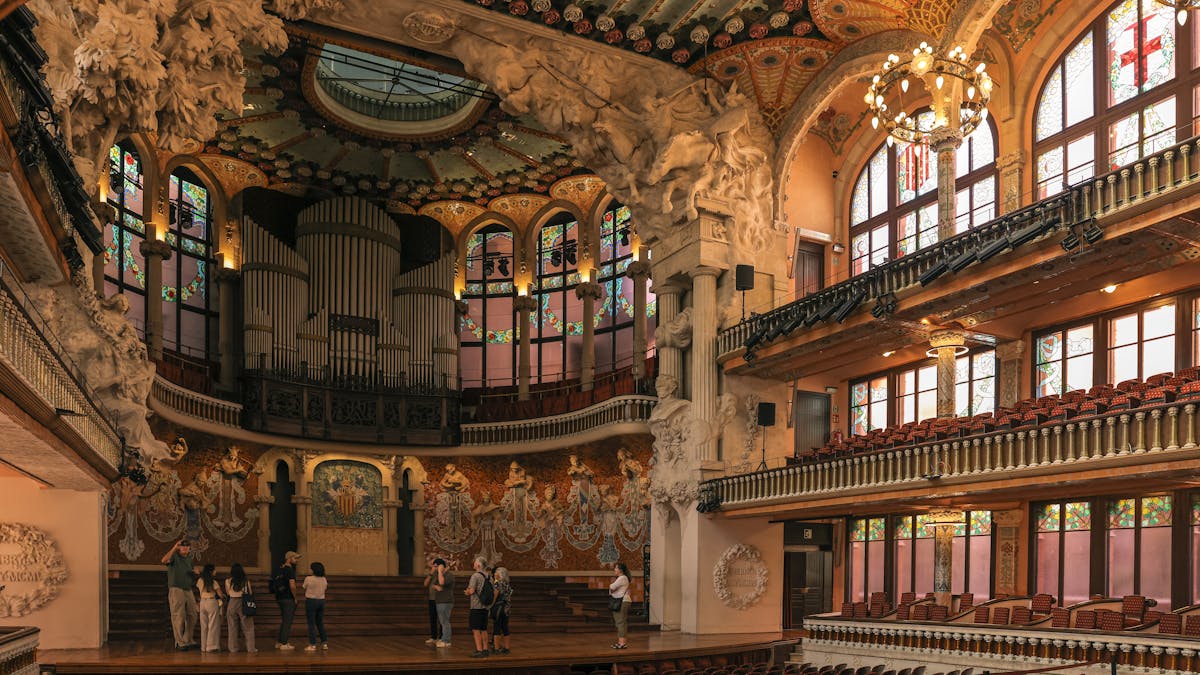 Interior of Palau de la Musica Catalana showing ornate columns and stained glass with visitors