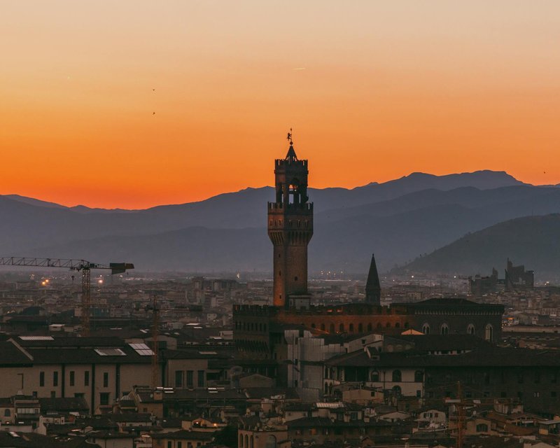 Stunning view of Palazzo Vecchio tower and Florence skyline against an orange sunset sky