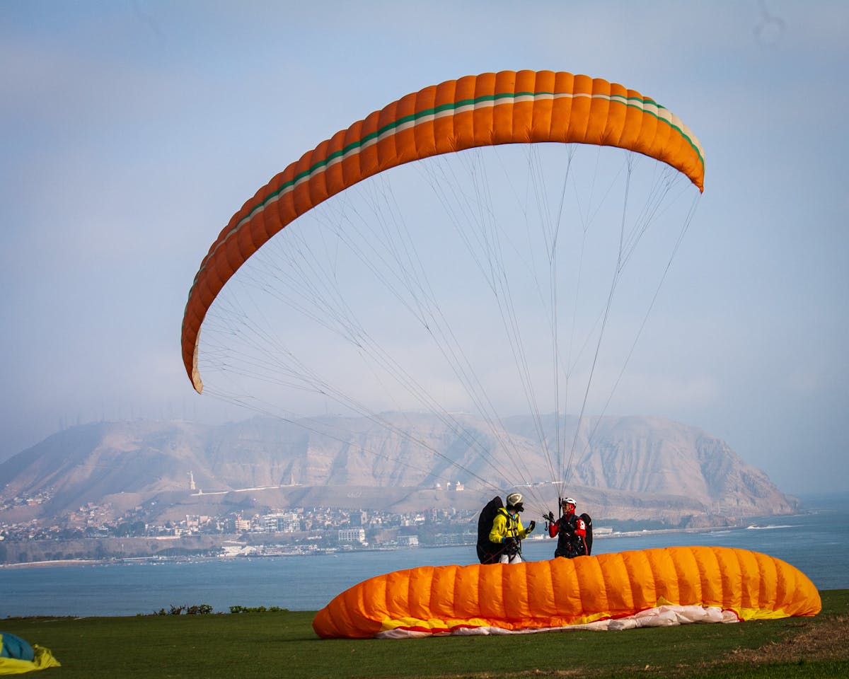 Two people with paragliding gear by scenic coastal cliffs