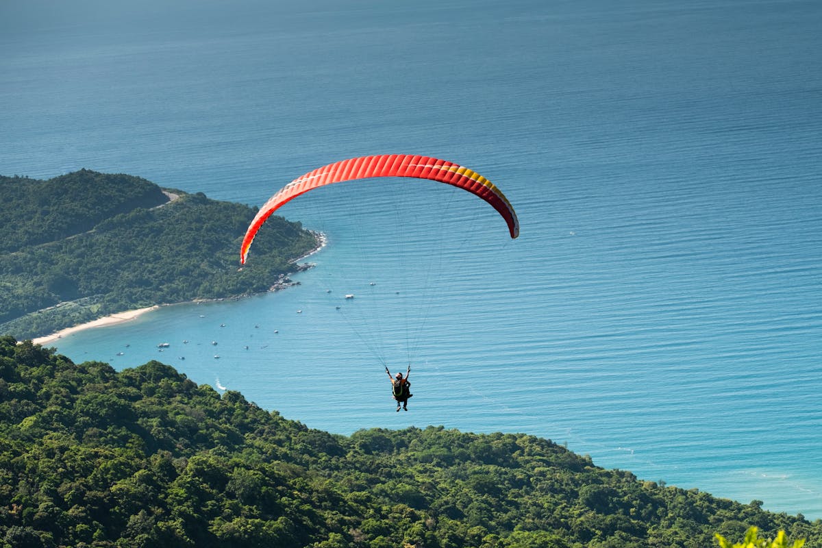 Paraglider soaring above forests with ocean in the distance