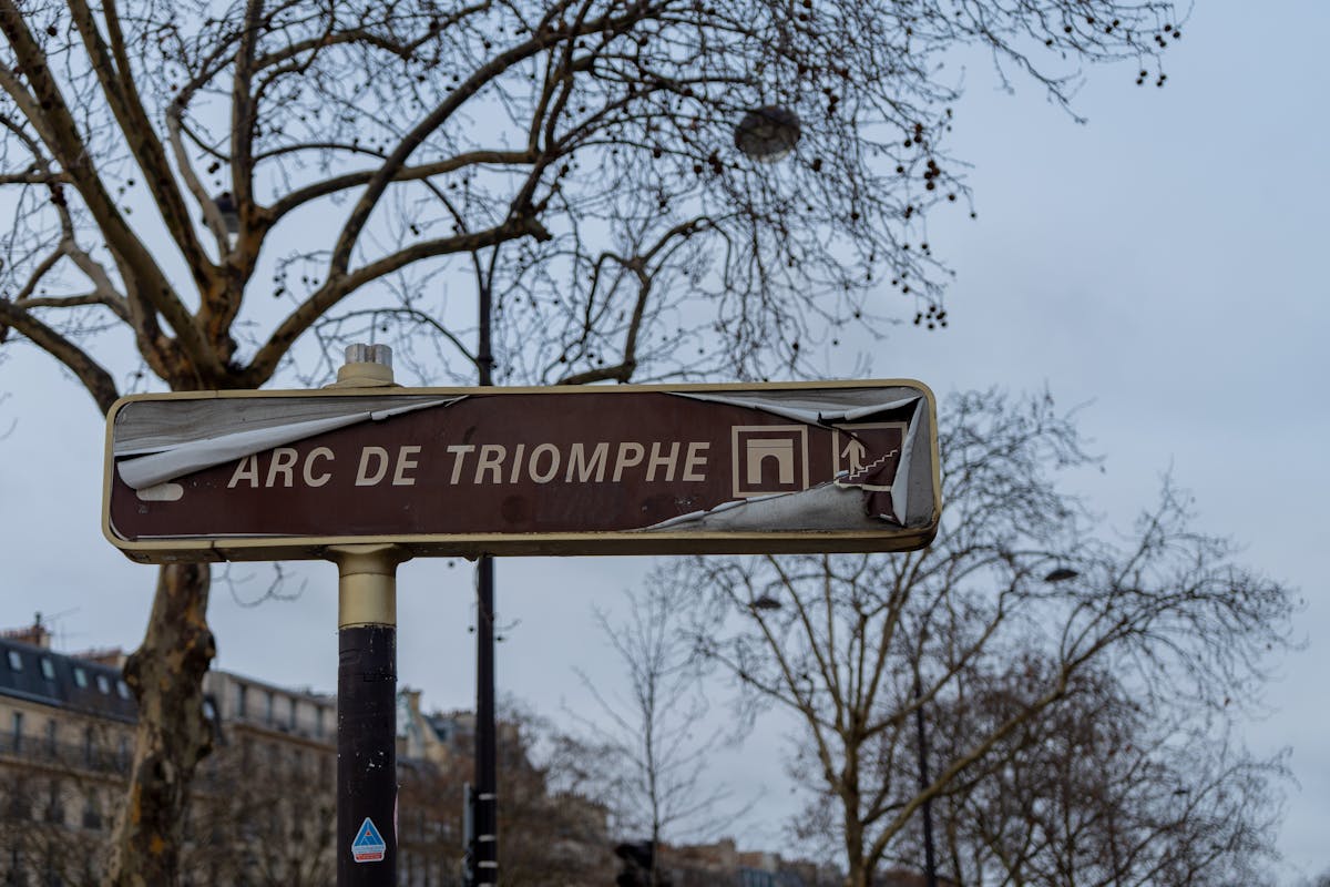 A weathered street sign pointing to the Arc de Triomphe in Paris