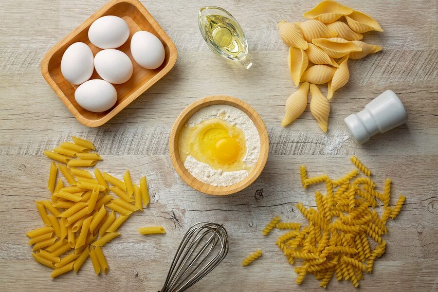 Flat lay of pasta ingredients including eggs flour and olive oil on a wooden surface