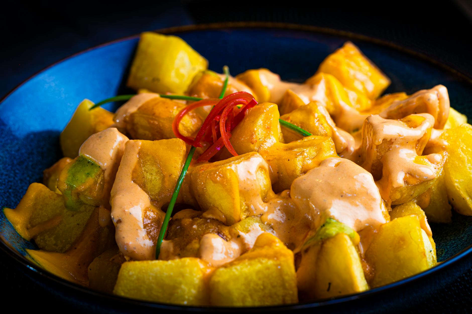 Close-up of patatas bravas with spicy aioli in a blue bowl