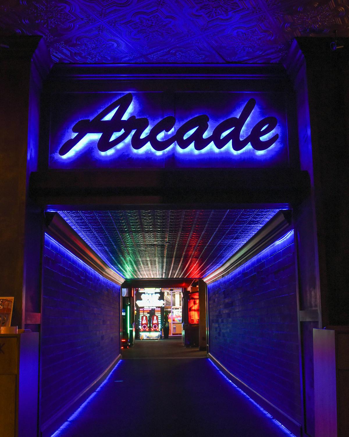 Neon-lit hallway leading to an arcade area with colorful lighting