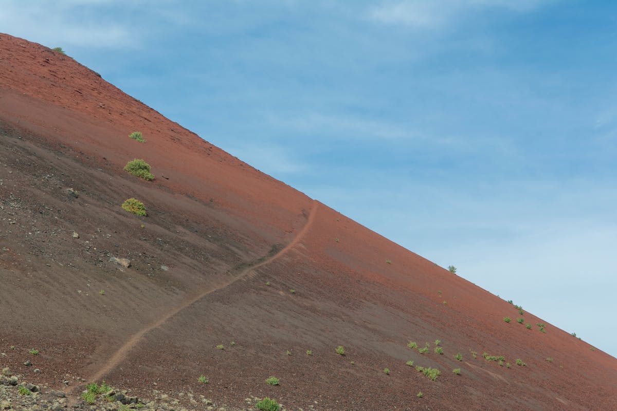 A winding dirt path leading up a volcanic hill with sparse vegetation in Lanzarote