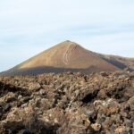 Rocky volcanic terrain stretching across Lanzarote with scattered dark lava rocks under cloudy skies