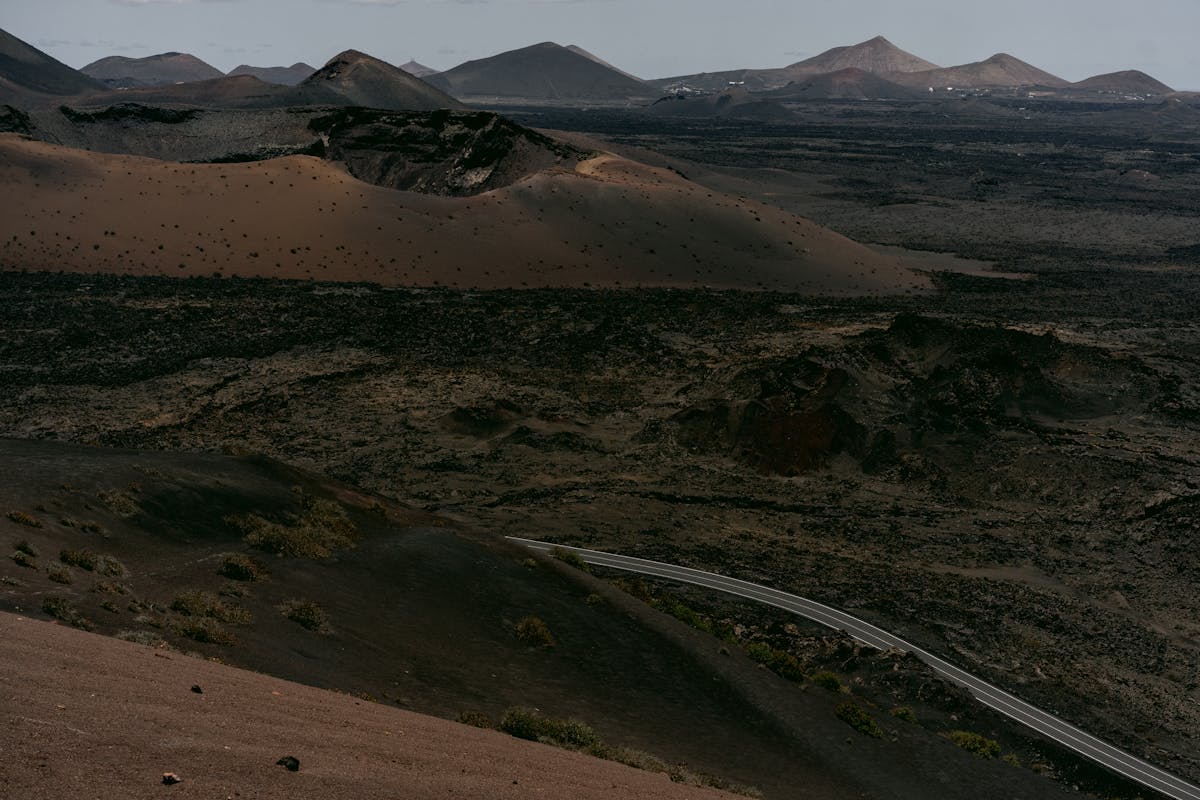 Aerial view of a road cutting through a stark volcanic landscape with barren terrain and mountains