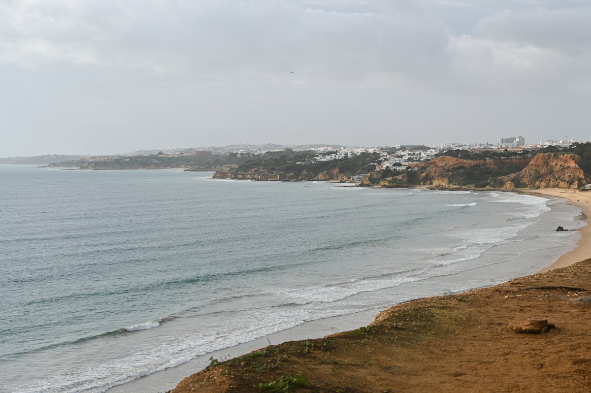 View of Faro coast with ocean waves cliffs and cloudy sky