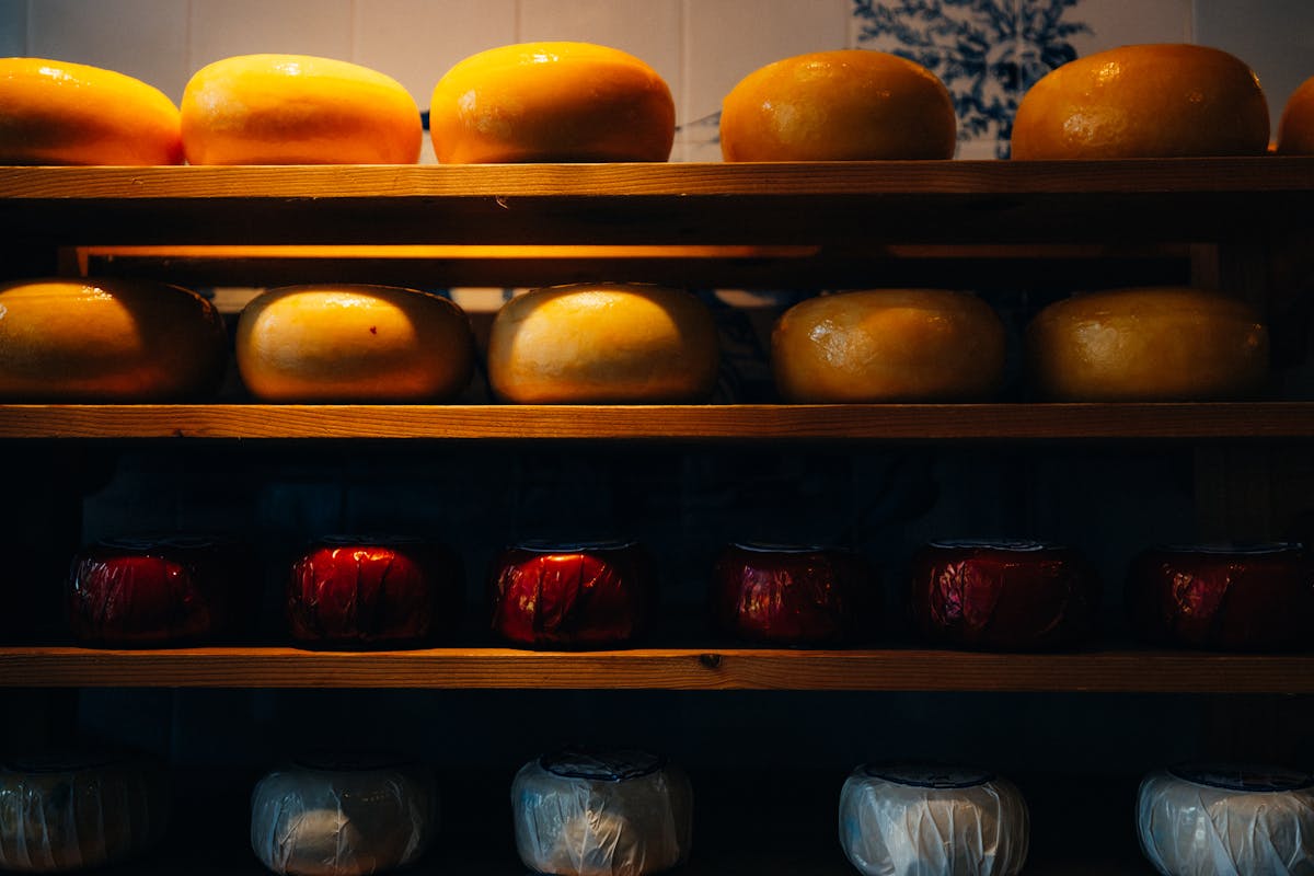 Variety of Gouda and Edam cheese wheels displayed on wooden shelves in an Amsterdam cheese shop