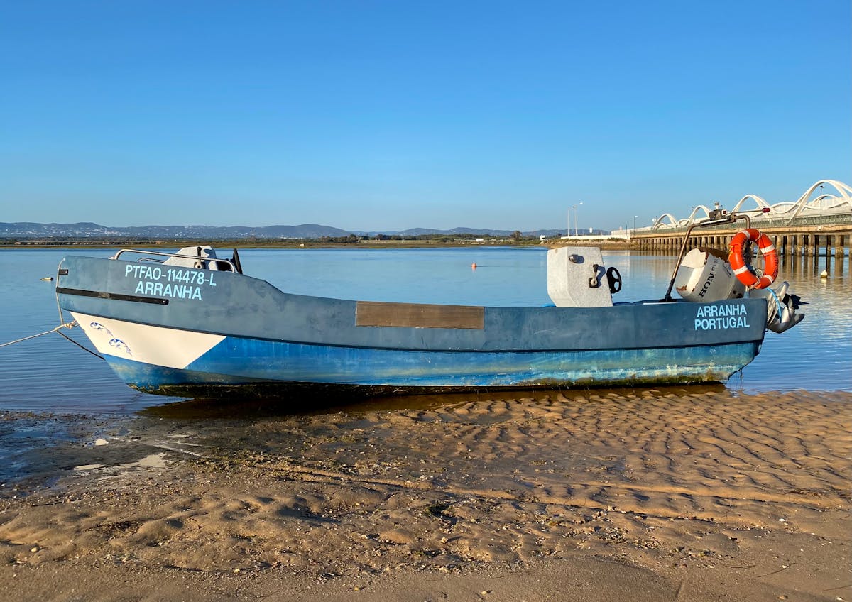 A blue fishing boat resting on the sandy shore in Faro, Portugal