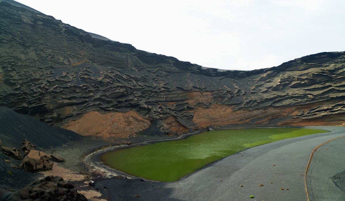A green crater lake surrounded by volcanic cliffs in Lanzarote