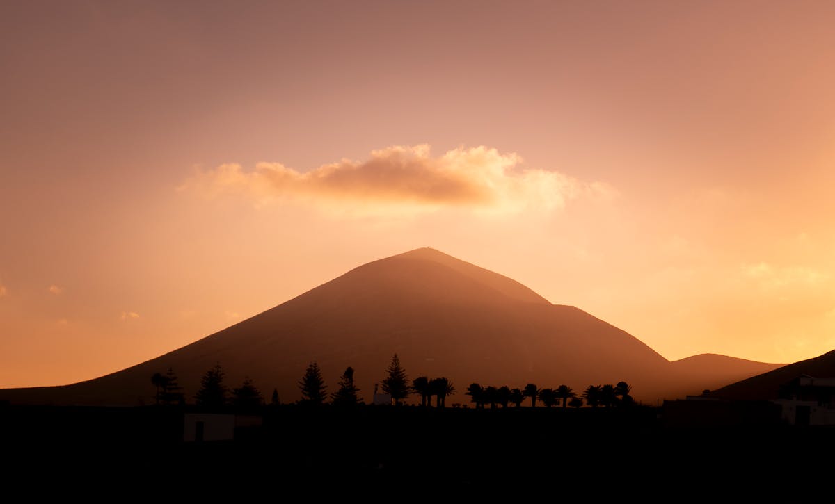 Silhouette of a volcanic peak in Lanzarote against an orange sunset sky