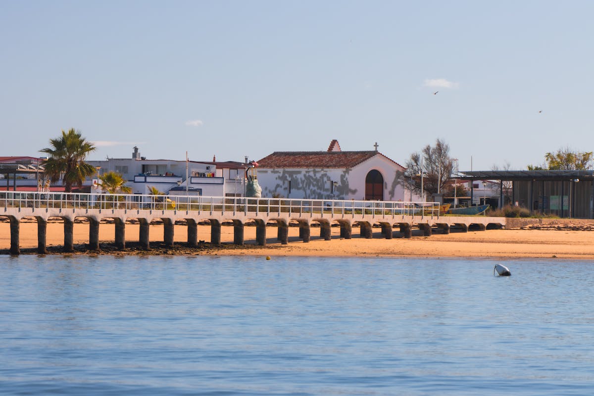 Sunny beach with coastal structures and people enjoying the sand in Faro, Portugal