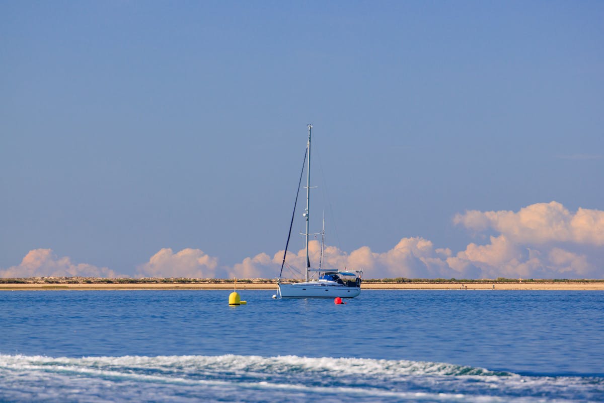 A sailboat anchored near the coast of Olhao Portugal under a clear blue sky