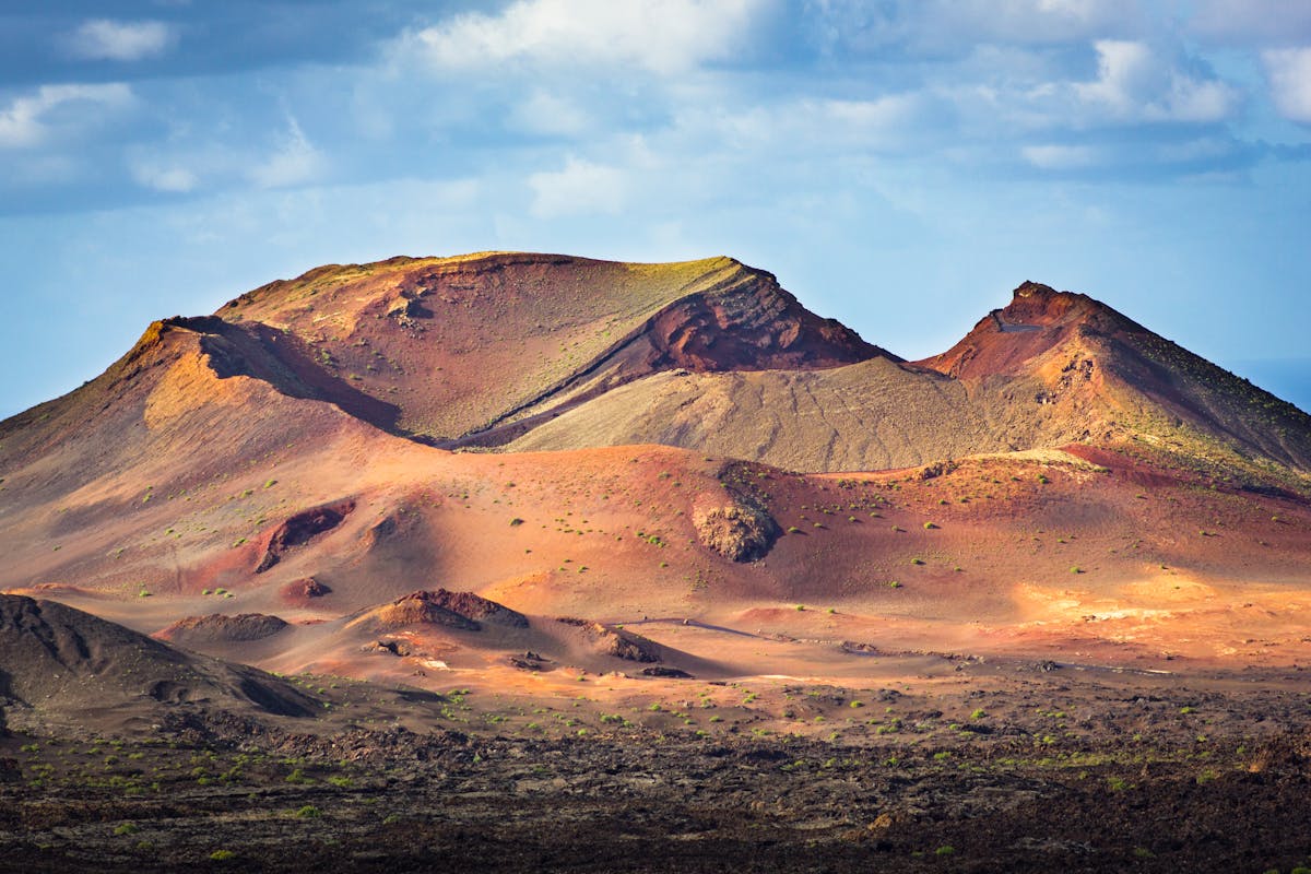 Volcanic mountains and terrain under cloudy sky in Timanfaya National Park Spain
