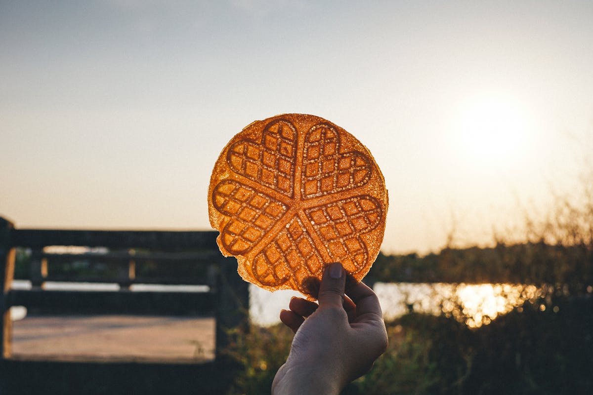 A hand holding a round waffle silhouetted against a golden sunset sky