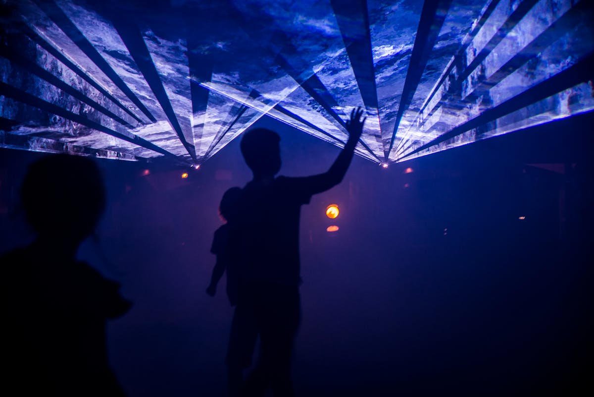 Silhouettes of people interacting with colorful light projections in a dark exhibition space